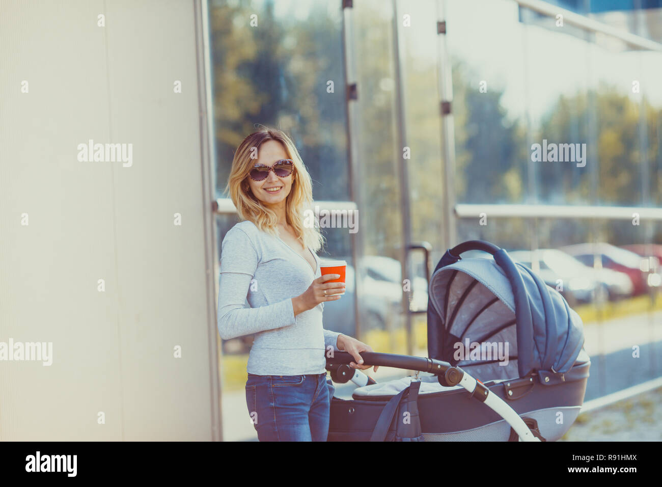 Trendy mother posing with cup of coffee and pram Stock Photo - Alamy