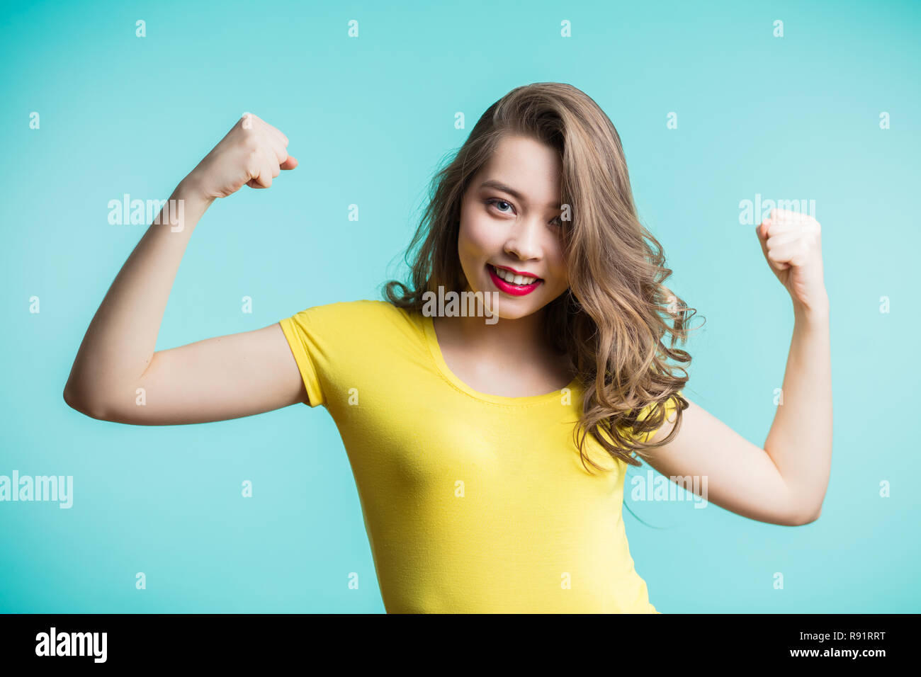 Portrait of cheerful young woman raising her fists with smiling ...
