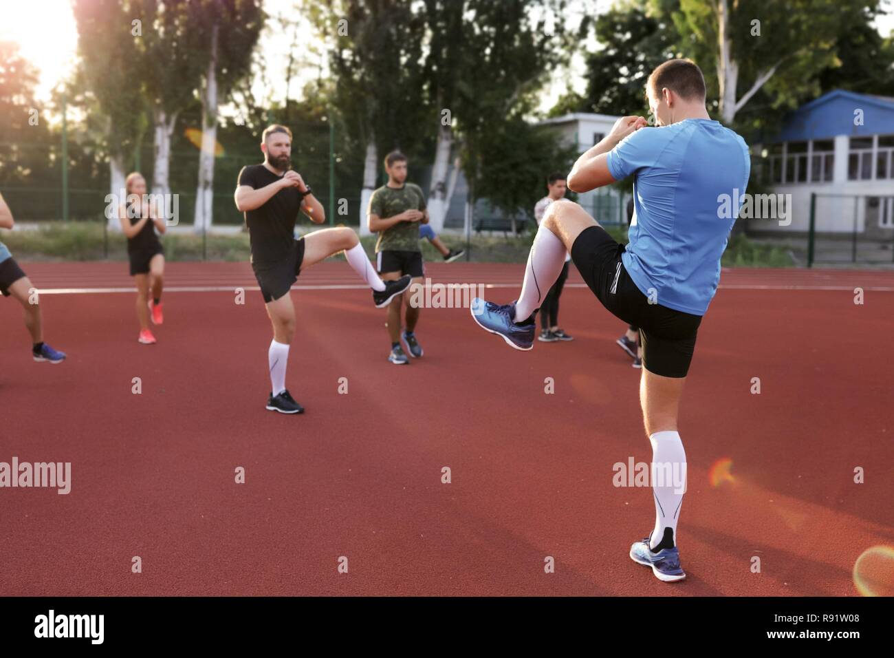 Coach trains people outdoor o the stadium. Do the warm up, kick legs up ...