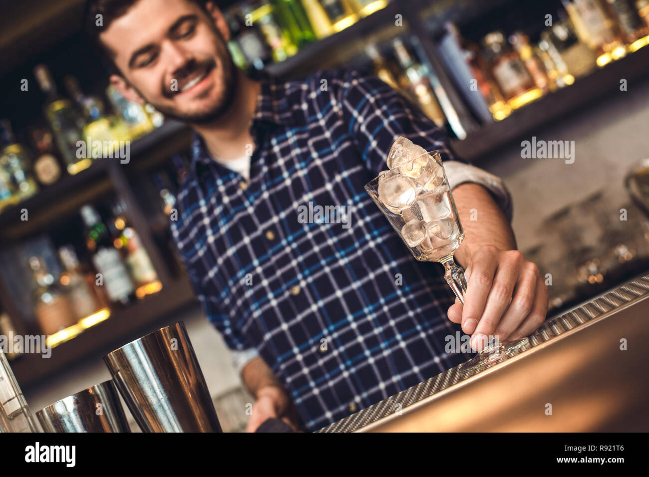 Young barman standing at bar counter serving glass with ice close-up ...