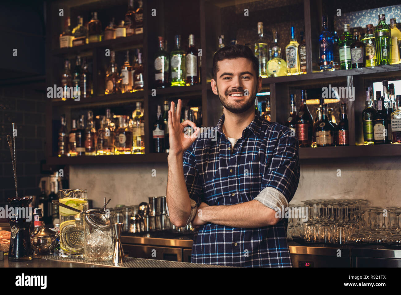 Young barman standing at bar counter showing ok sign looking camera ...