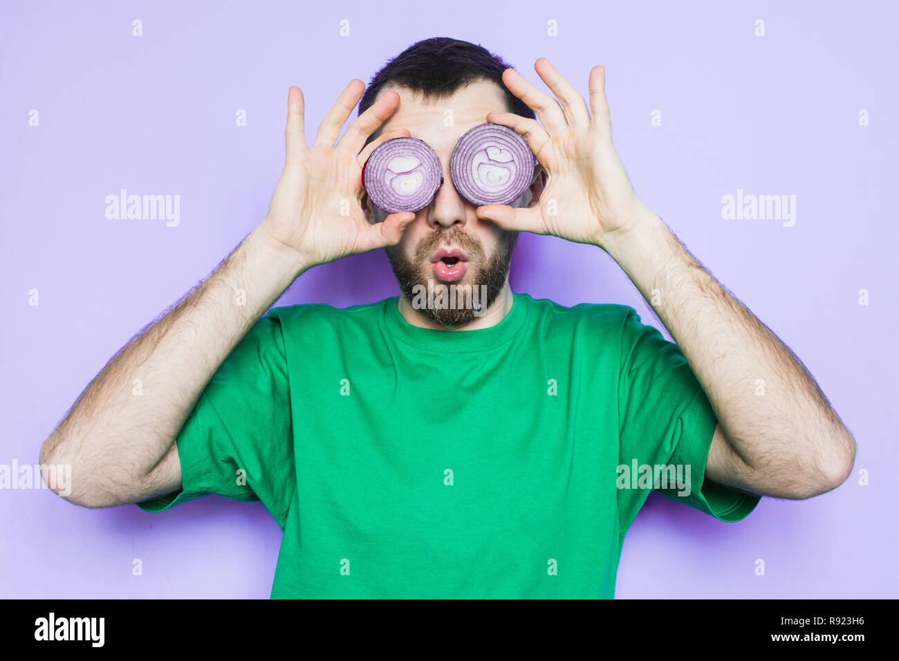 Young bearded man holding slices of red onion in front of his eyes ...