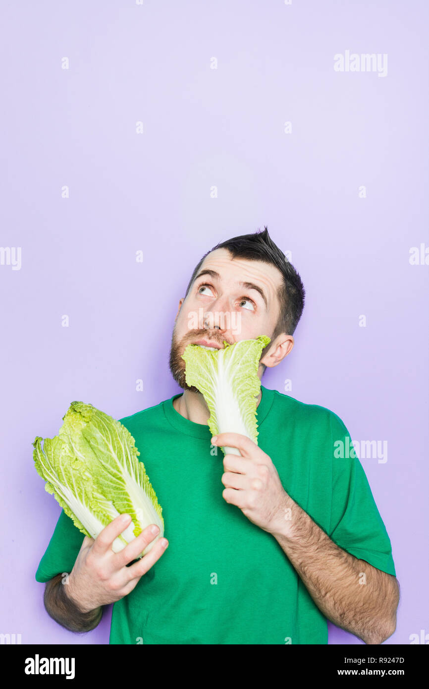 Young man biting on a leaf of Beijing napa cabbage, doubt face ...