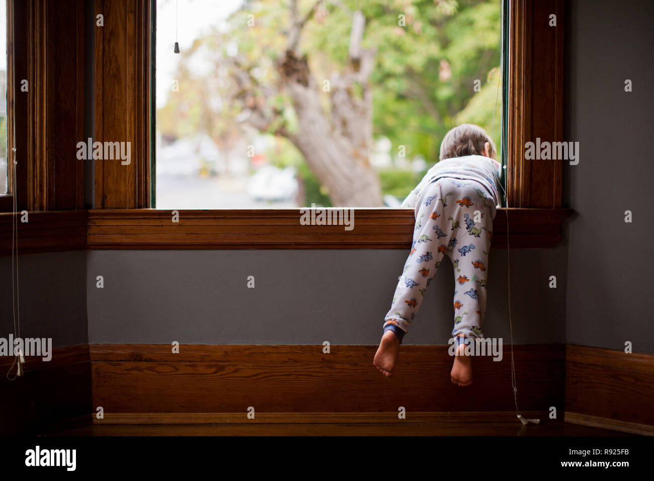 Young boy in pajamas looking out a window Stock Photo - Alamy