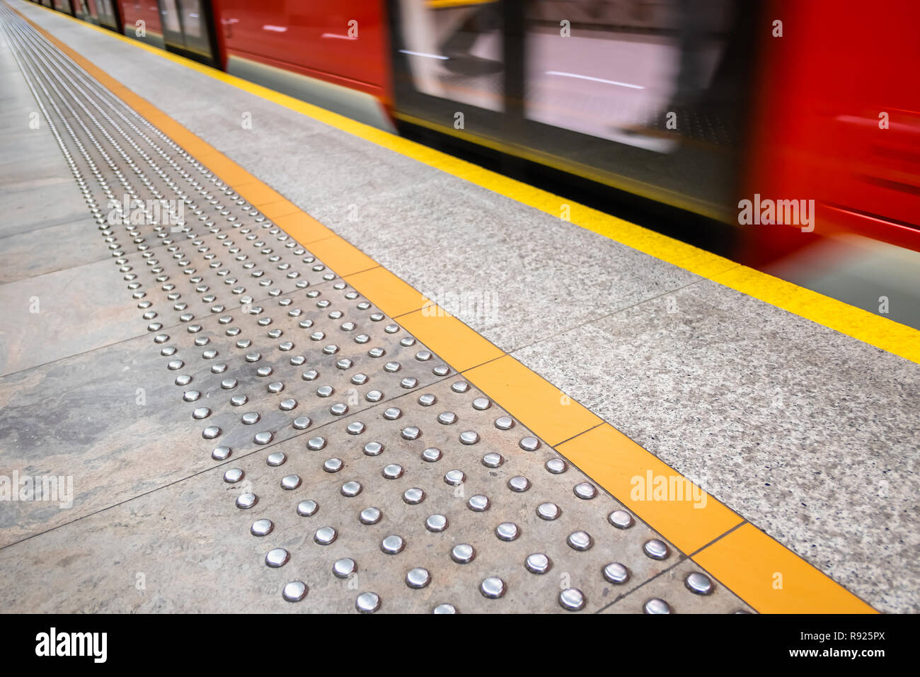 blurred red subway train, diagonal tactile paving also called ...