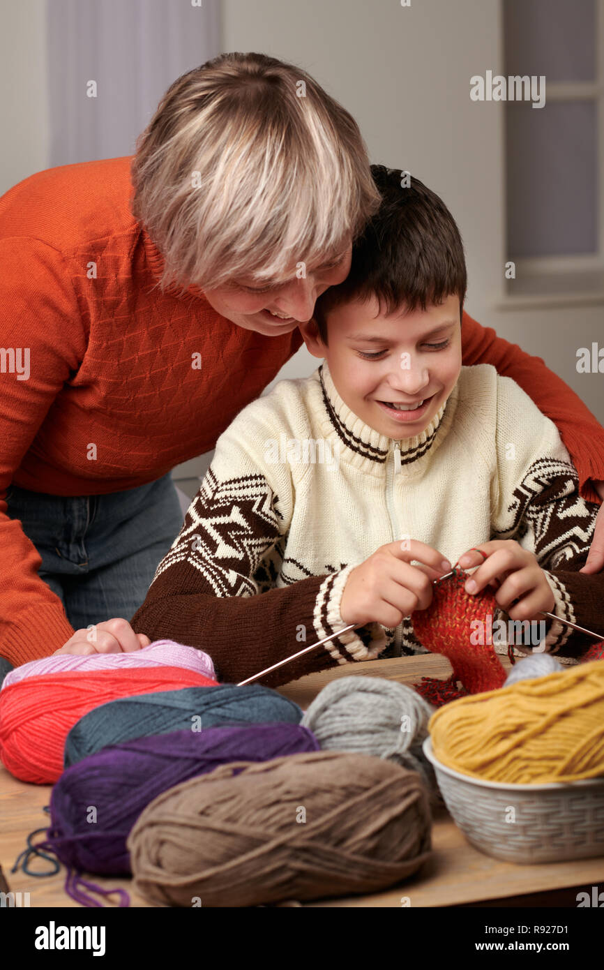 Mother is learning her child boy to knit. Colorful wool yarns are on ...