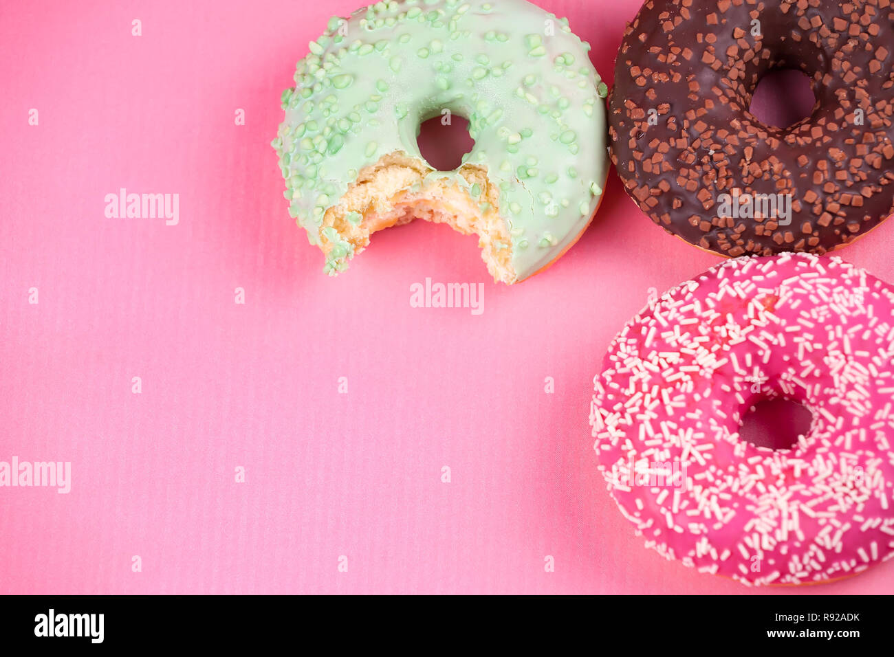 Sweet colorful tasty donuts with icing and sprinkles on pastel pink ...