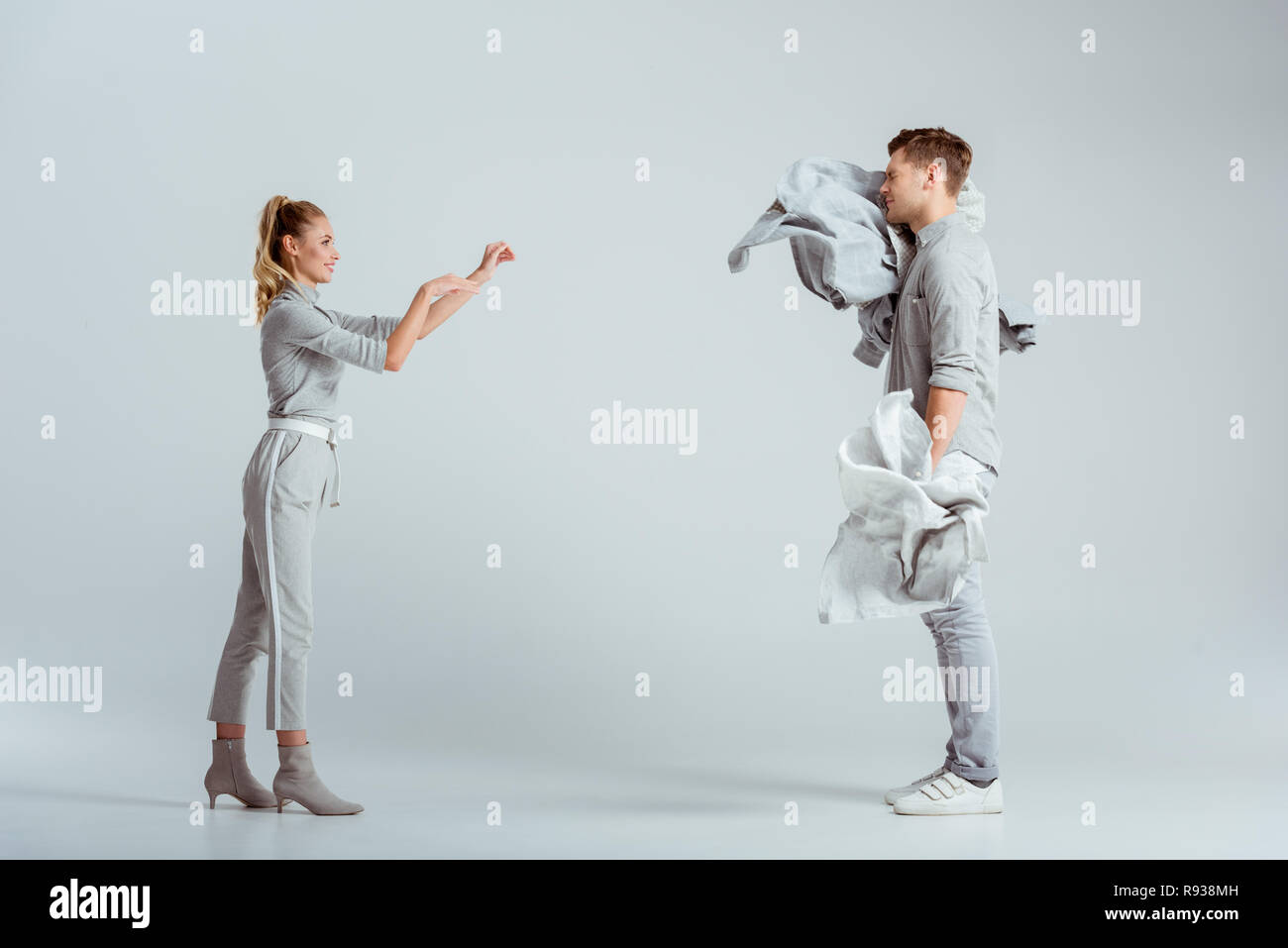 attractive woman throwing pile of clothes at man on grey background ...