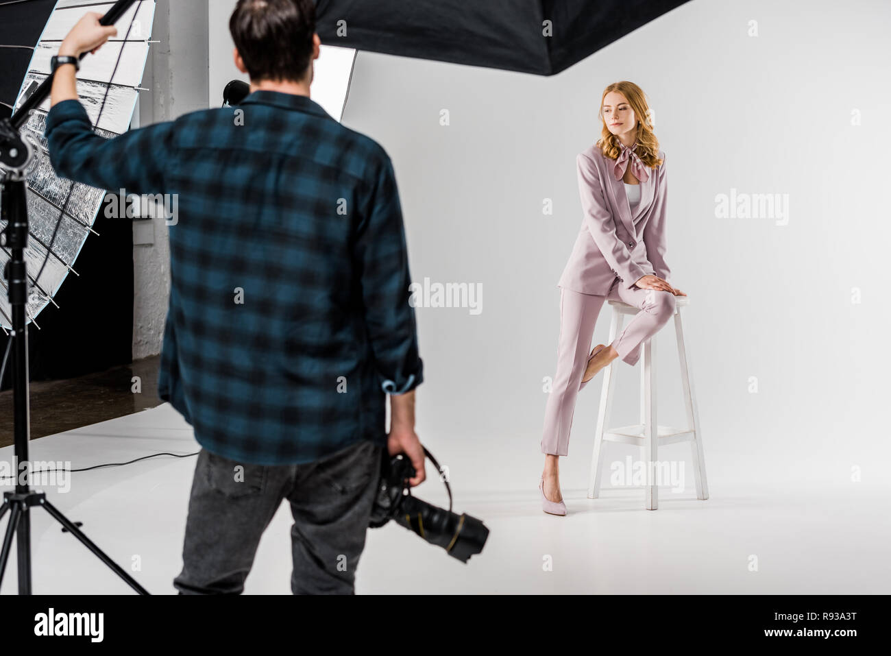 back view of photographer holding camera and model posing in studio ...
