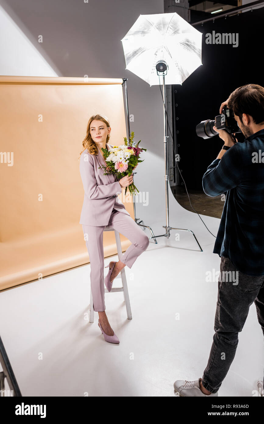 photographer shooting attractive young female model posing with flowers ...