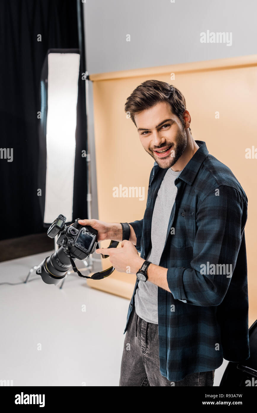 handsome happy young photographer pointing at camera in photo studio ...