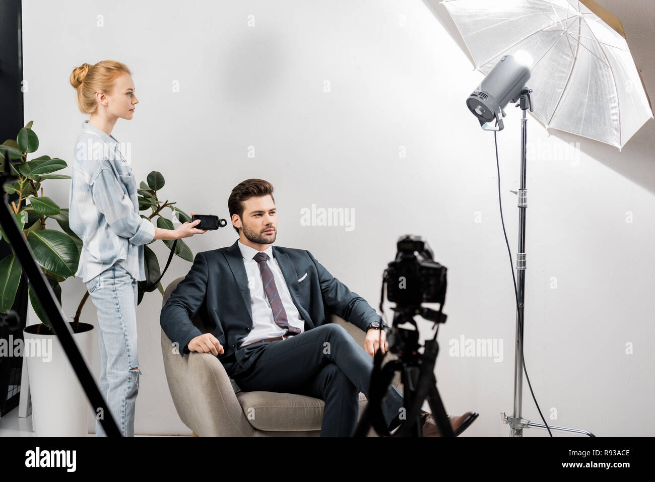 young photographer using light meter while working with handsome male ...