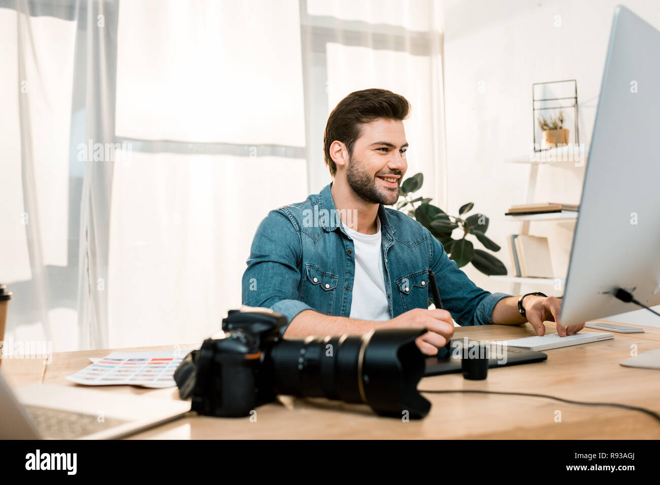 smiling young photographer using desktop computer and retouching photos ...
