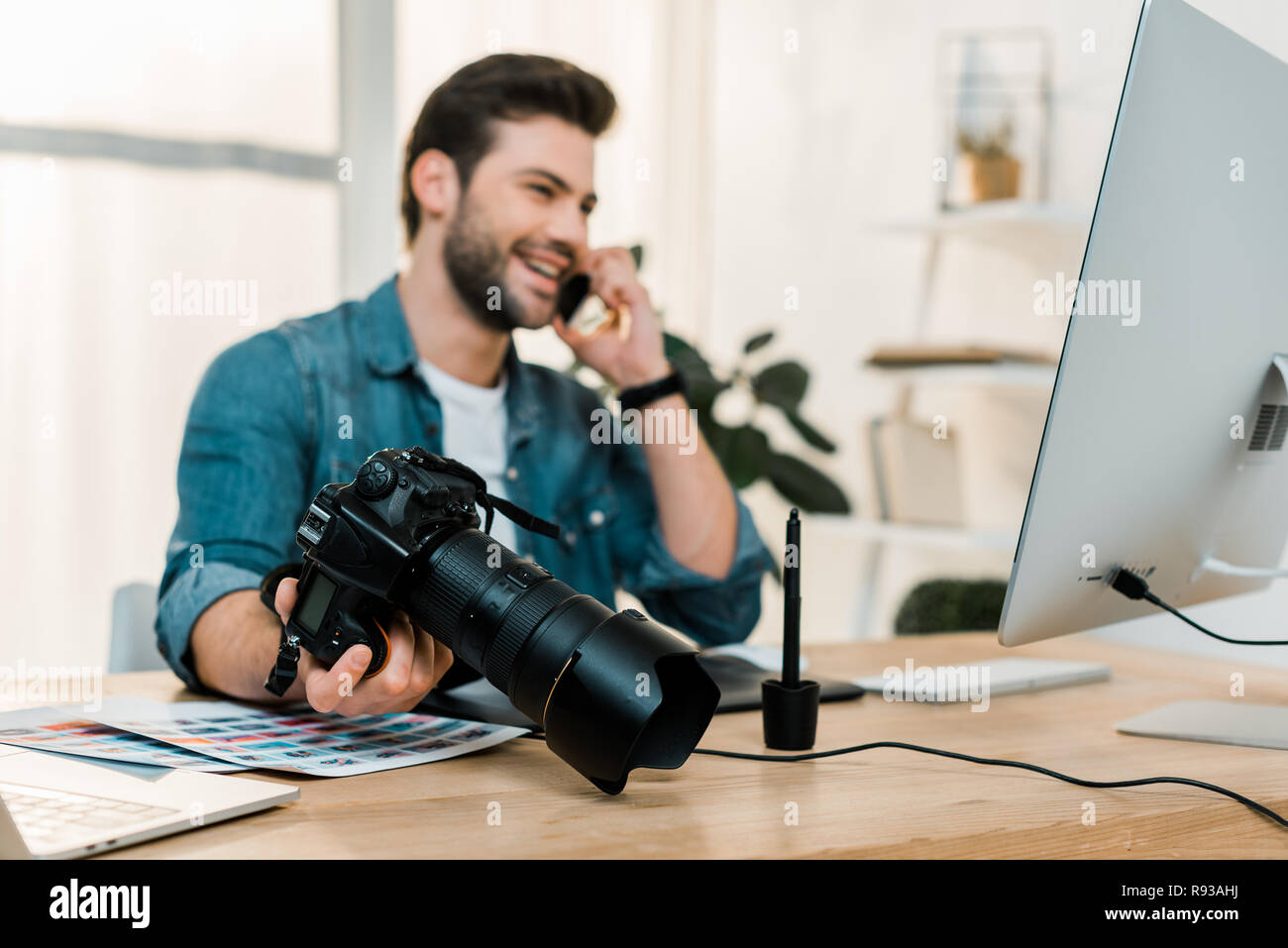 happy young photographer holding camera and talking by smartphone at ...