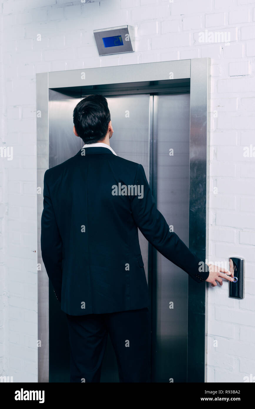 back view of man in black suit pressing elevator button Stock Photo - Alamy