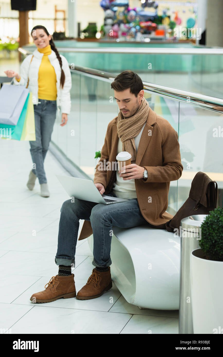 handsome man sitting on bench,holding disposable cup and typing laptop ...