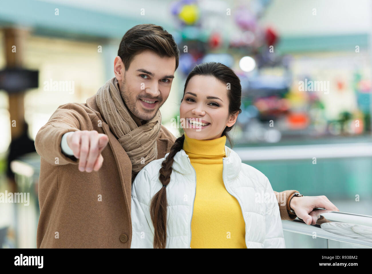 handsome man pointing with finger at camera ad smiling girl in shopping ...