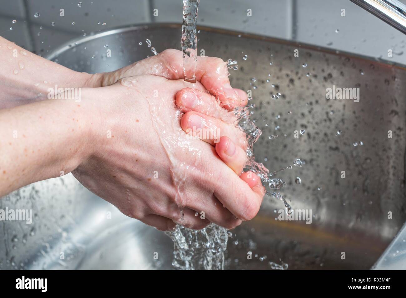 Person washing their hands under running water from a faucet, symbolic ...