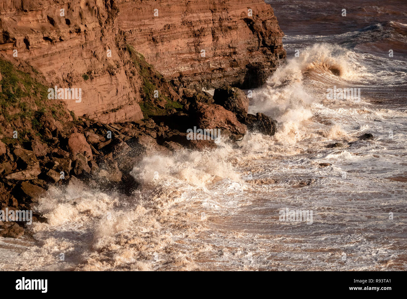 Waves crashing into the red sandstone cliffs of the Jurassic Coast ...