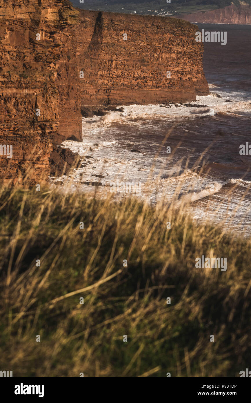 Waves crashing into the red sandstone cliffs of the Jurassic Coast ...