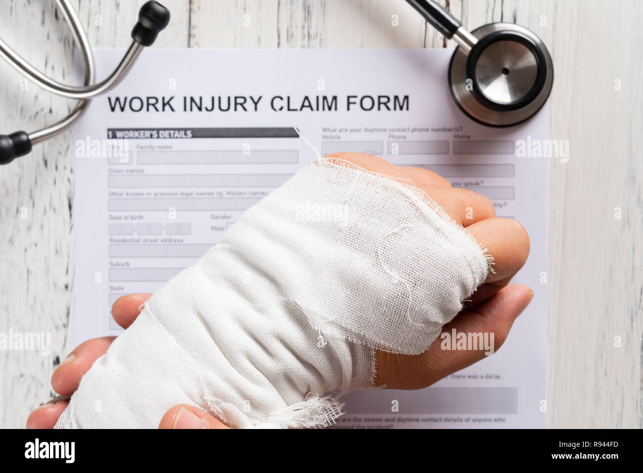 man holding his wrapped hand on top of a work injury claim form with ...