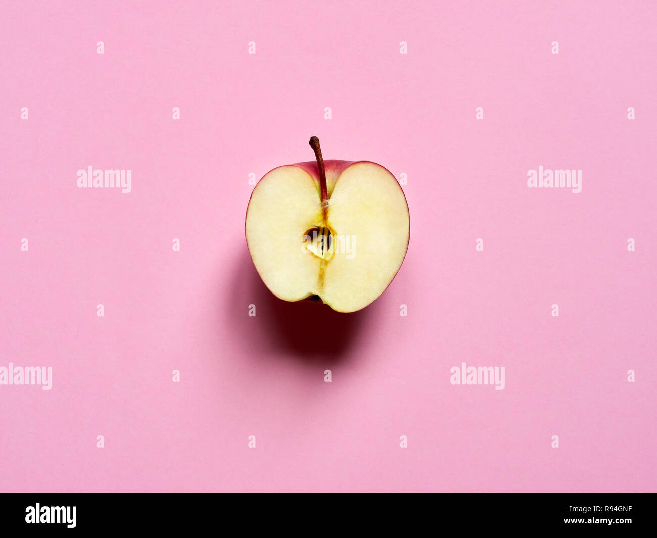 Apple fruit sliced by half isolated in studio over a light pink ...