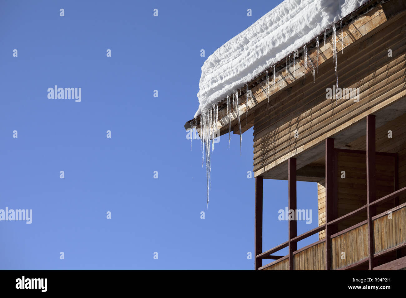 Roof with snow cornice and icicle at wooden house with balcony and ...