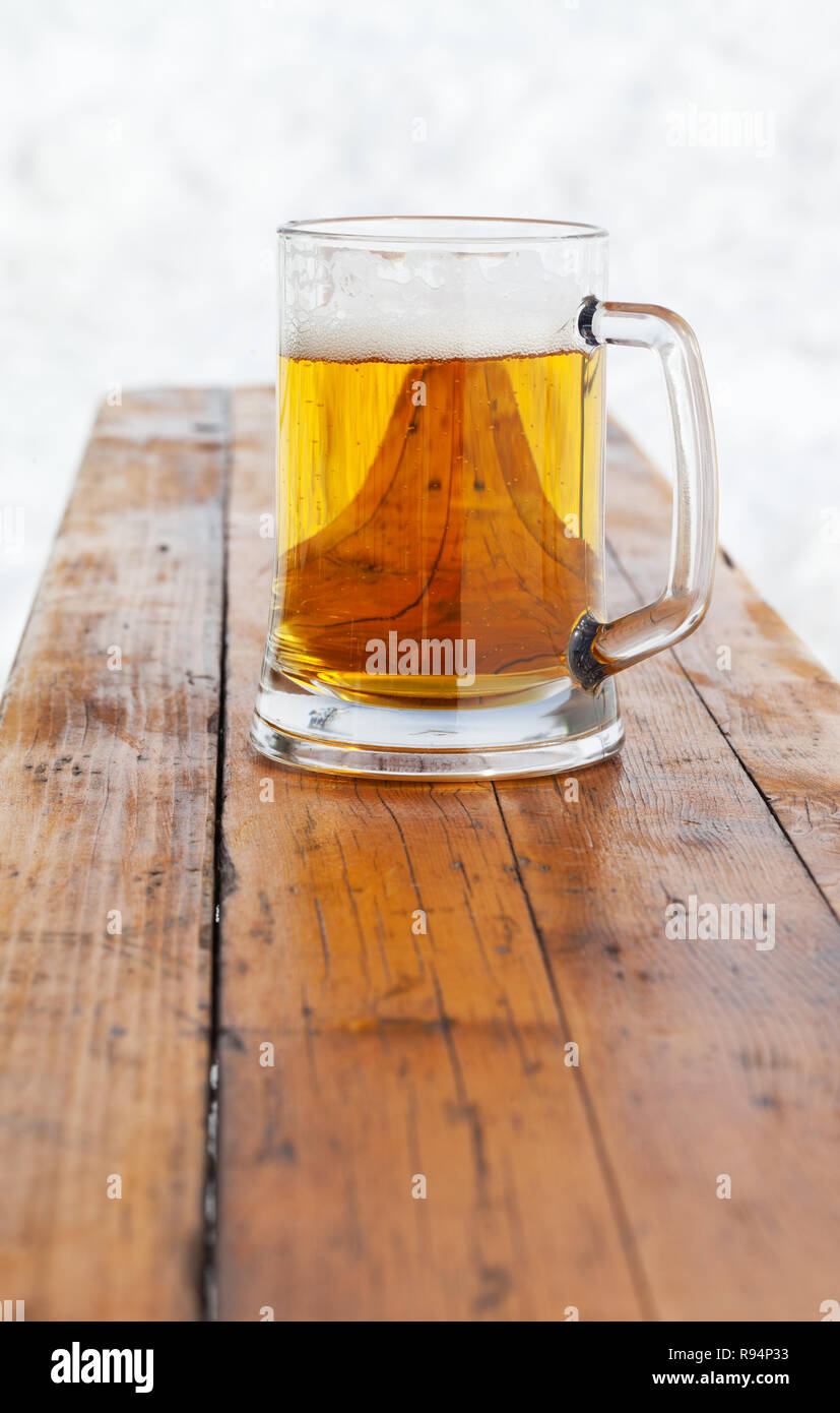 Glass mug with fresh cold beer on wooden bench in winter outdoor cafe ...