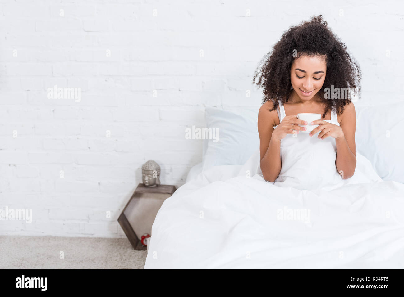 happy curly african american girl holding cup of coffee in bed during ...