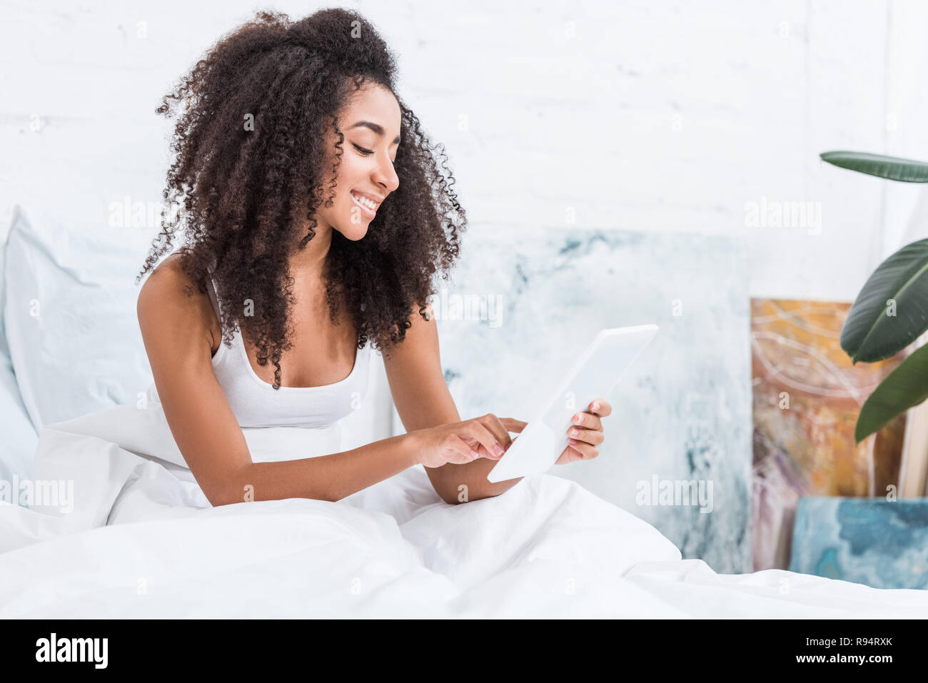 happy african american young woman using digital tablet in bed during ...