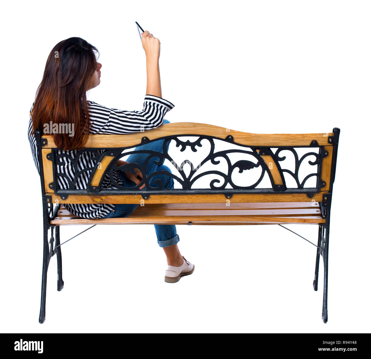 back view of woman sitting on bench and looks at the screen of the ...