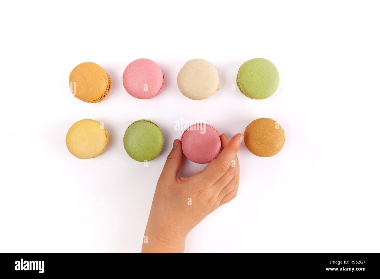 Girl's hand taking pink French macaron from two rows of colorful ...
