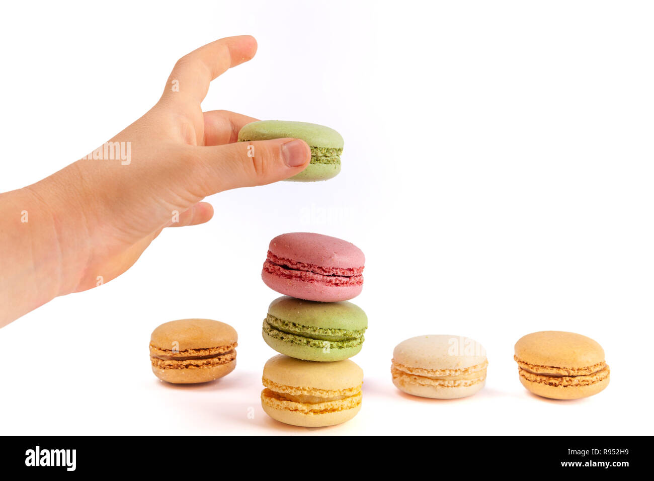 Child's hand placing green macaron on tower of colorful French macarons ...