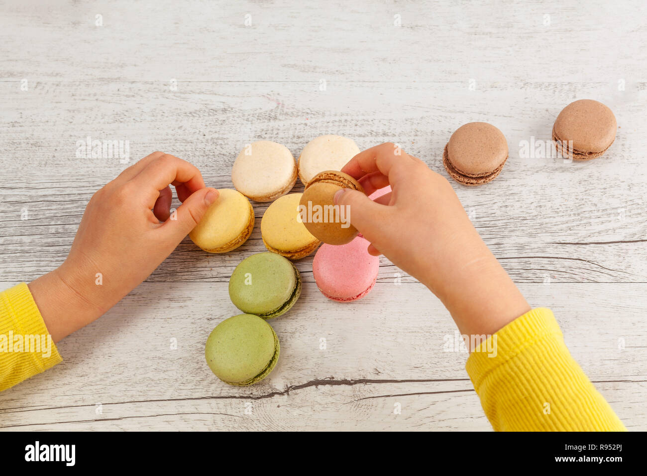 Child's hands playing with macarons on white rustic wooden table Stock ...