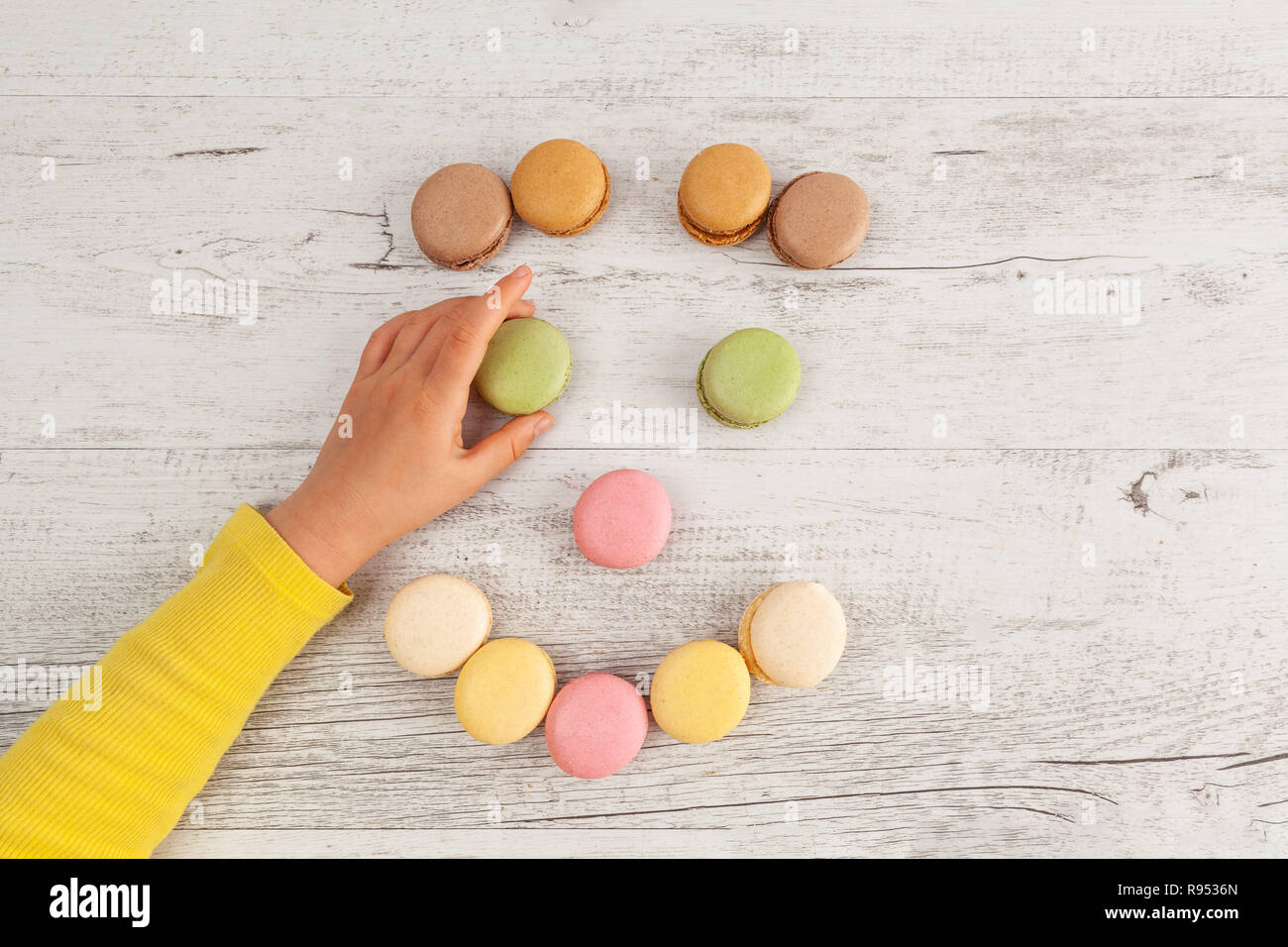 Child placing an eye on smiley face made from macarons with copy space ...