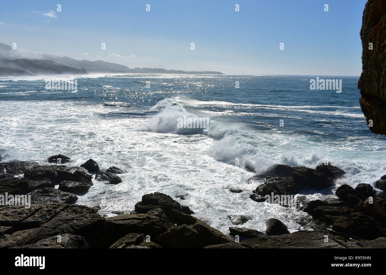 Big waves from a cliff. Rocks, wild sea with foam and mist. Blue sky ...