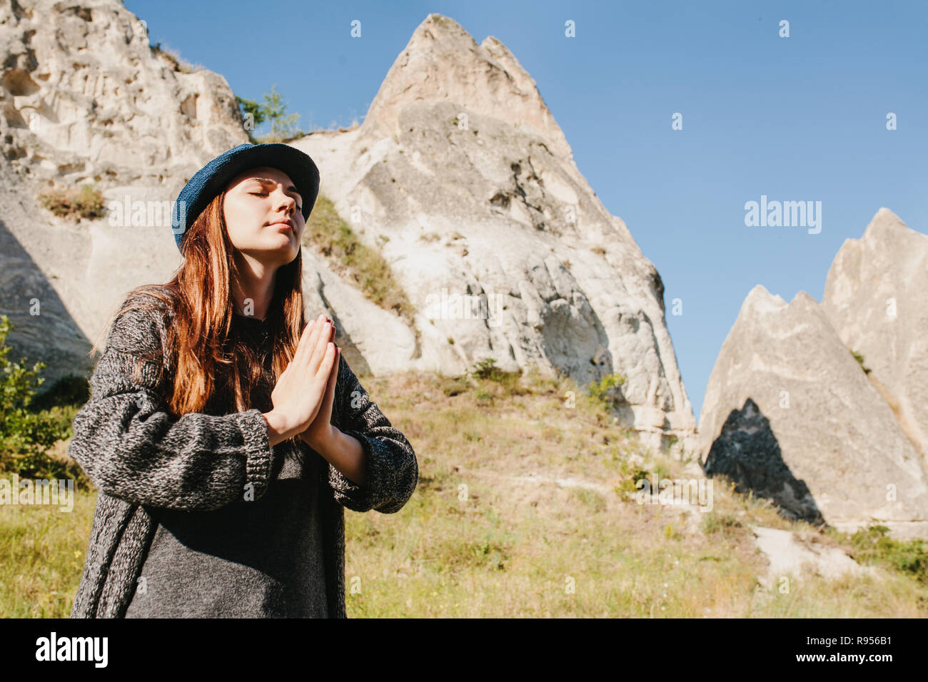 Beautiful young woman in hat and gray sweater meditates with folded ...