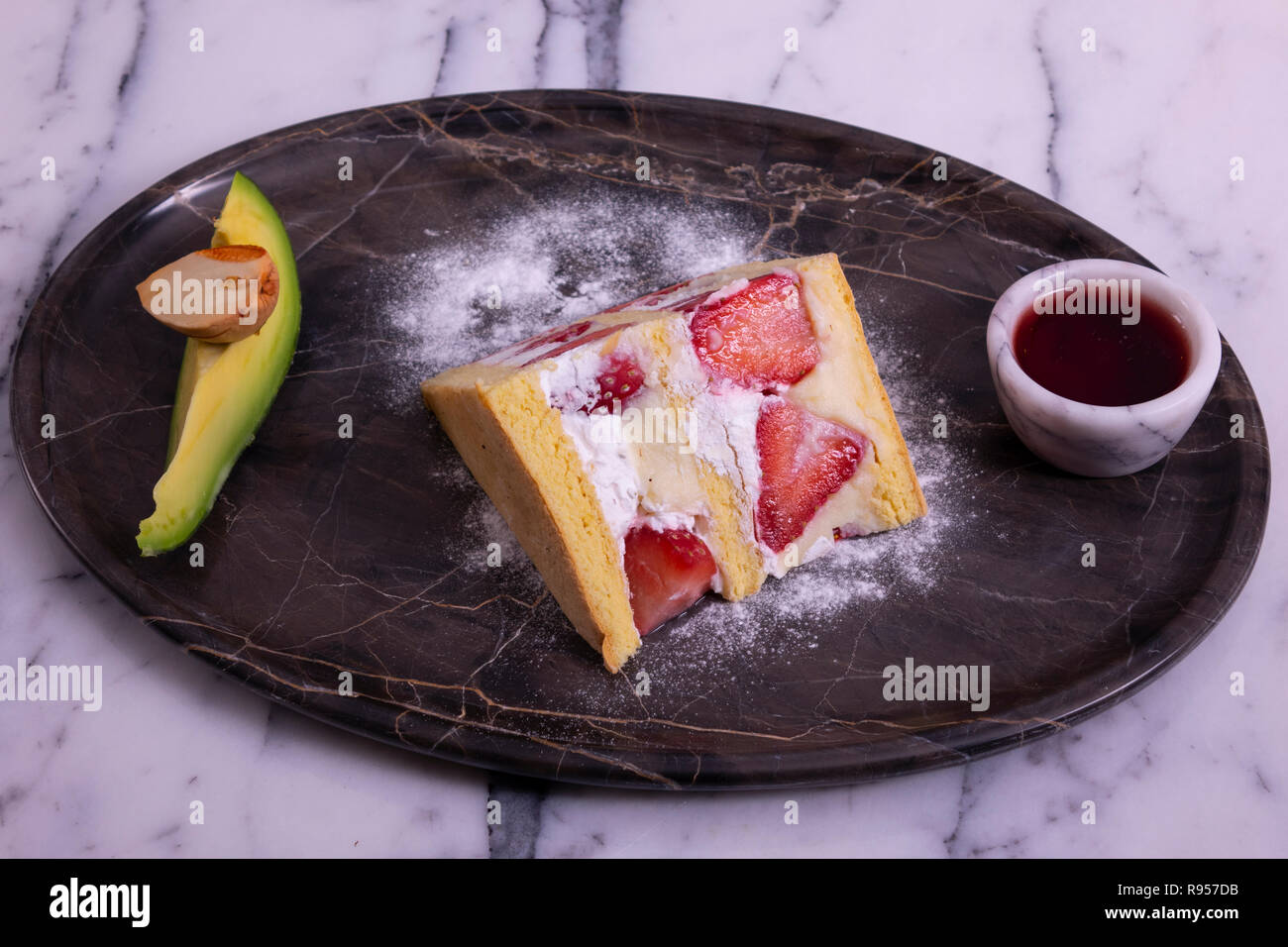 Strawberry cake and alligator pear in black marble plate on white ...