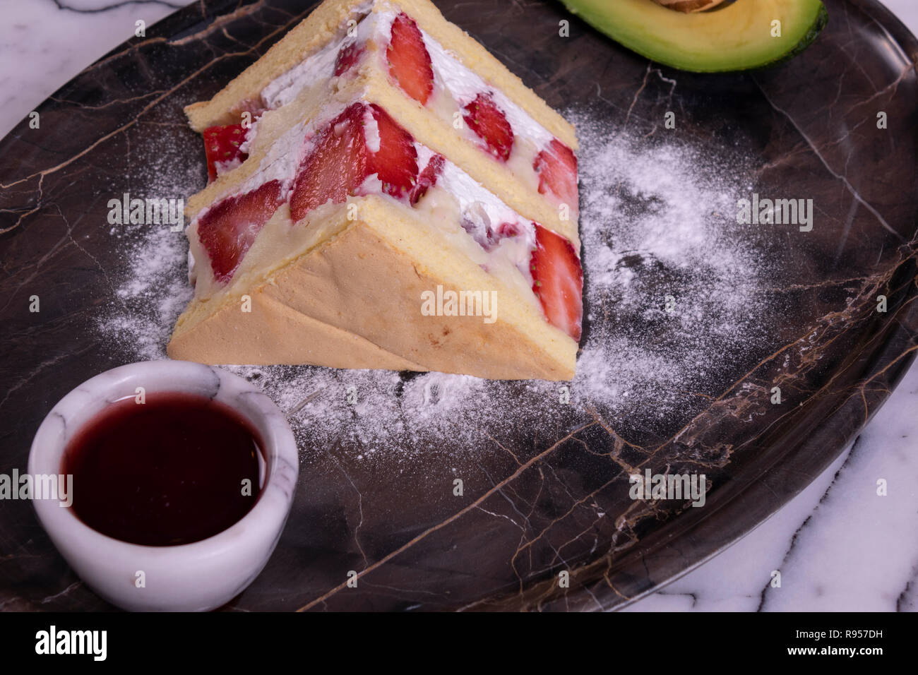 Strawberry cake and alligator pear in black marble plate on white ...