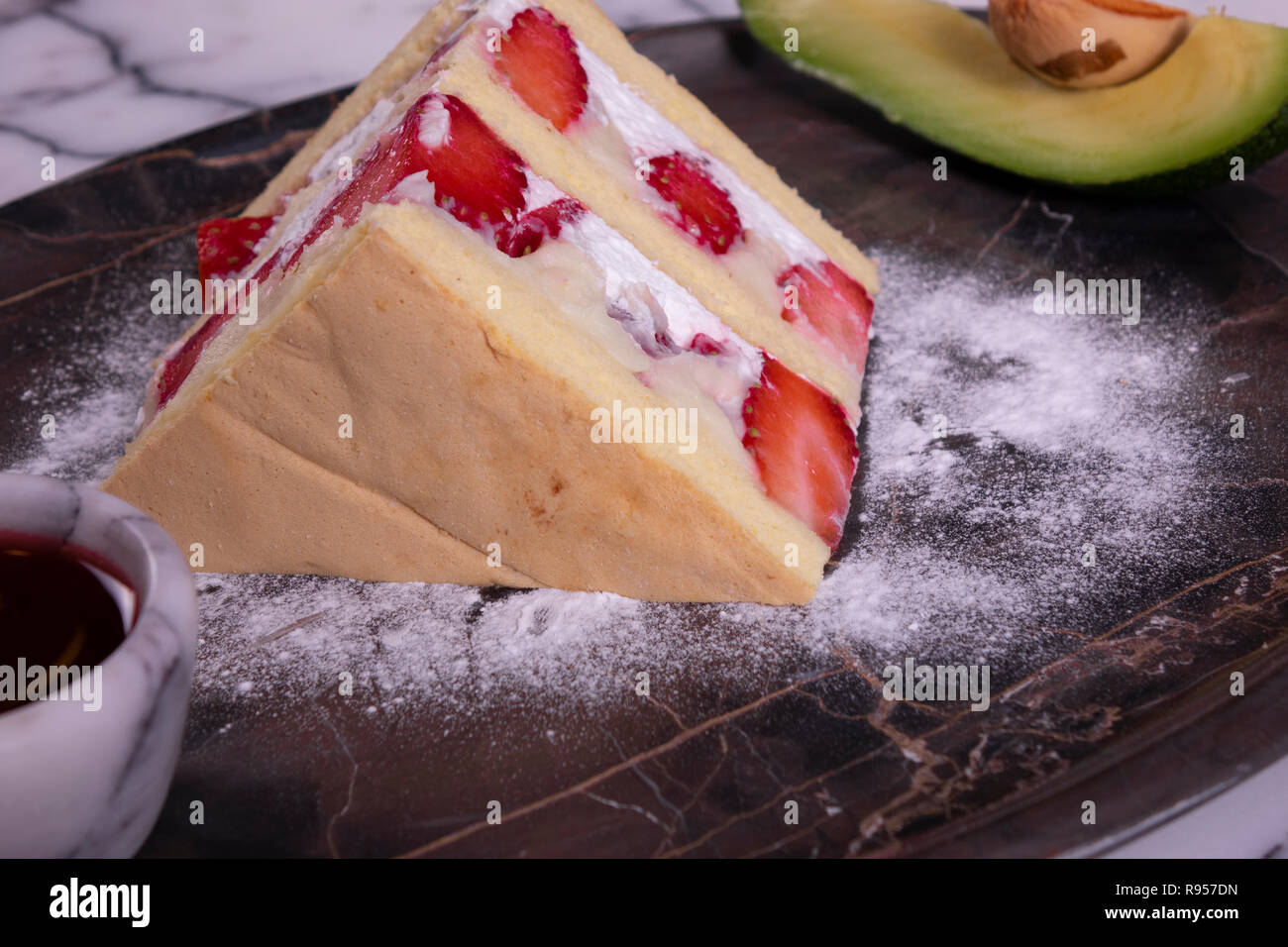Strawberry cake and alligator pear in black marble plate on white ...