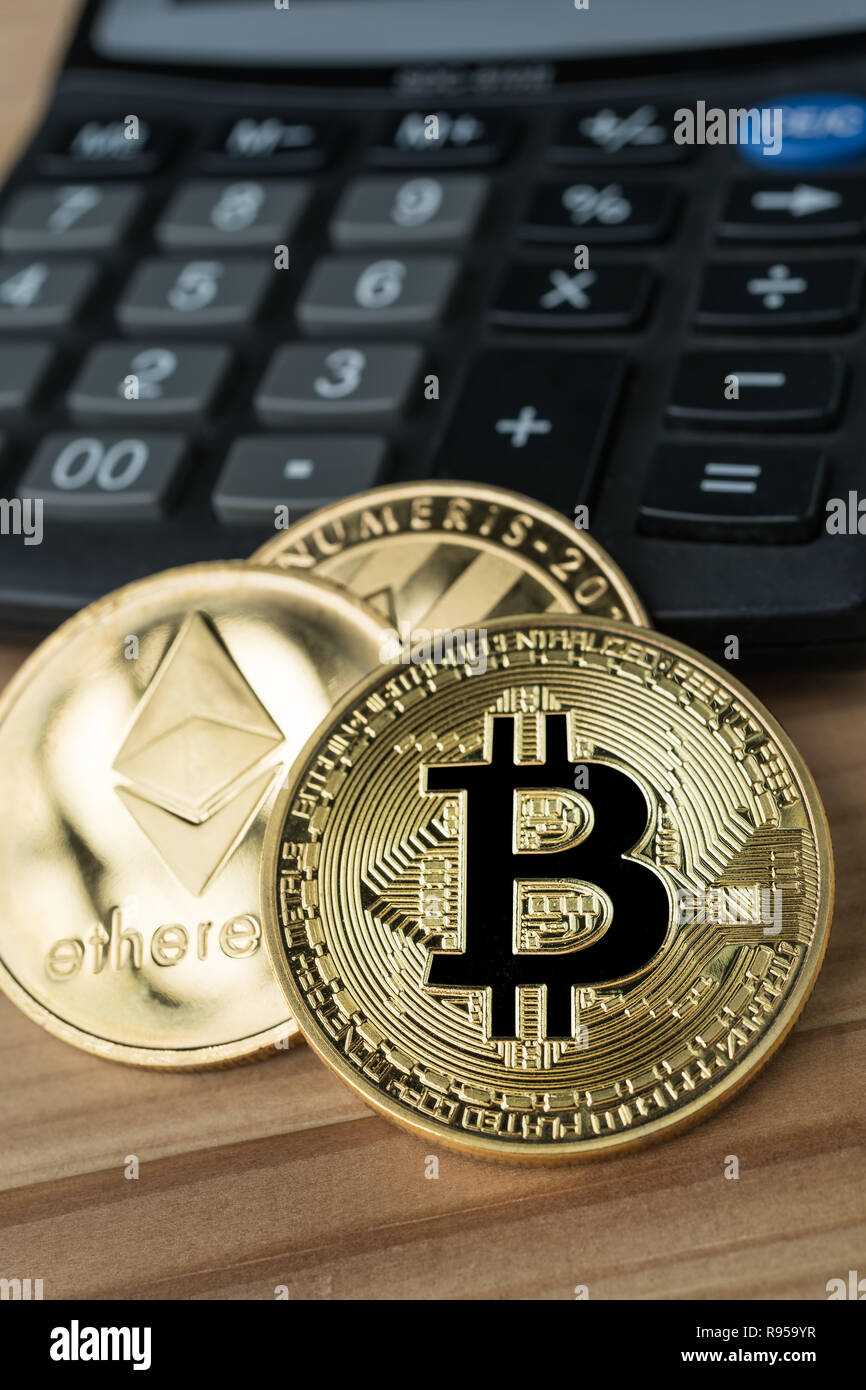 Golden physical Bitcoin, Ethereum and Litecoins on calculator on wooden ...