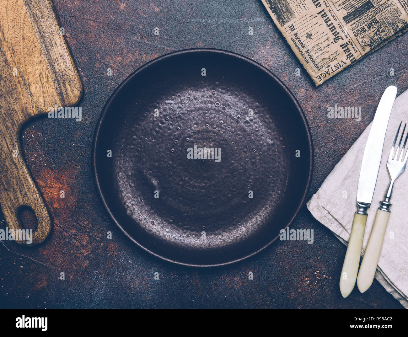 Empty brown plate (ceramic) on a dark background with a knife and fork ...