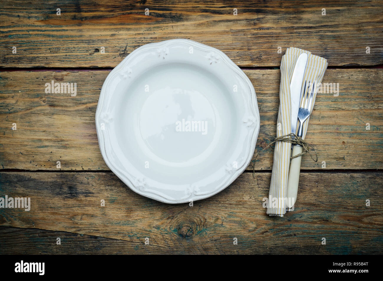 Empty white rustic plate on old wooden background with knife, fork and ...