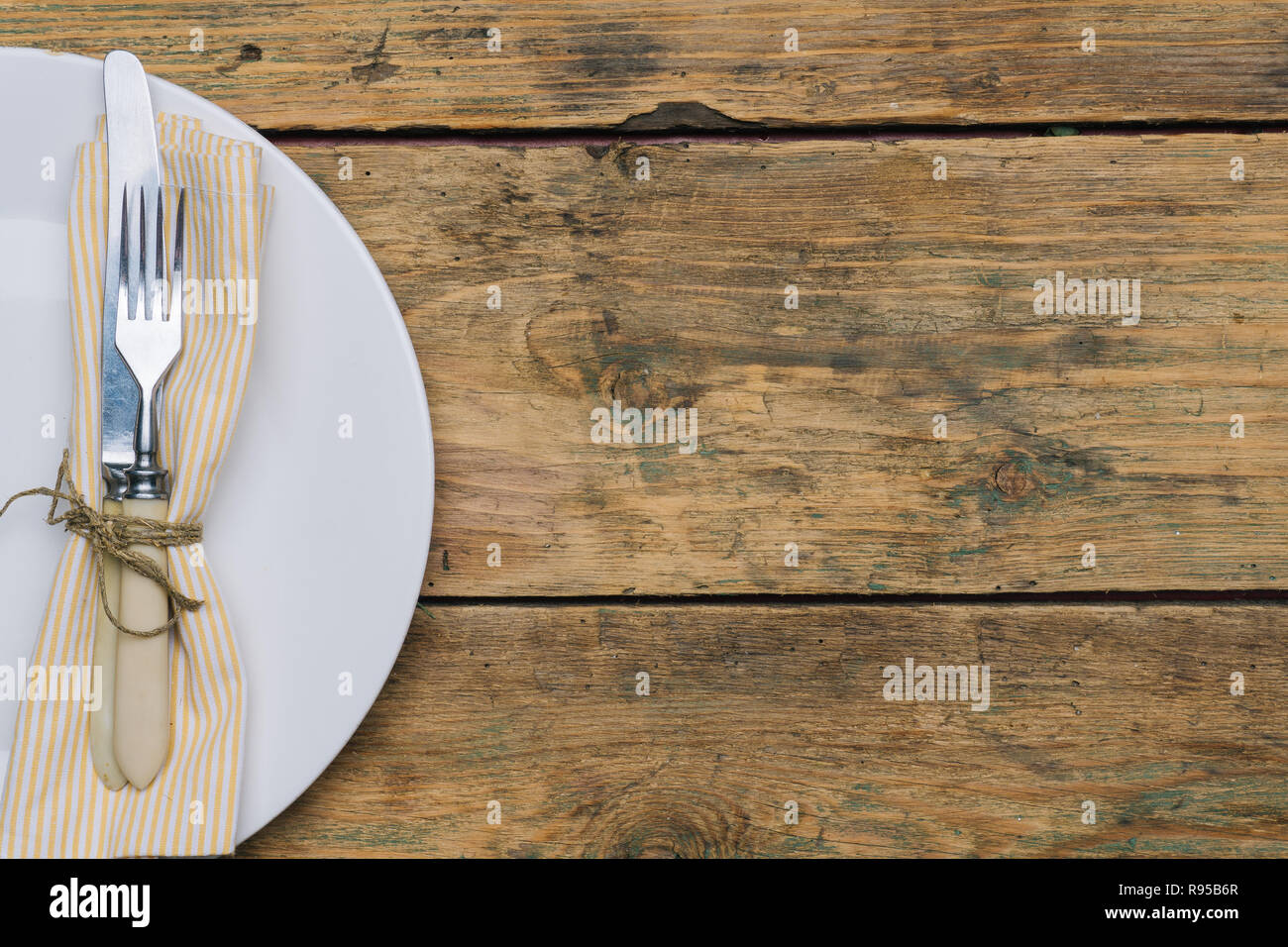 Empty white rustic plate on old wooden background with knife, fork and ...