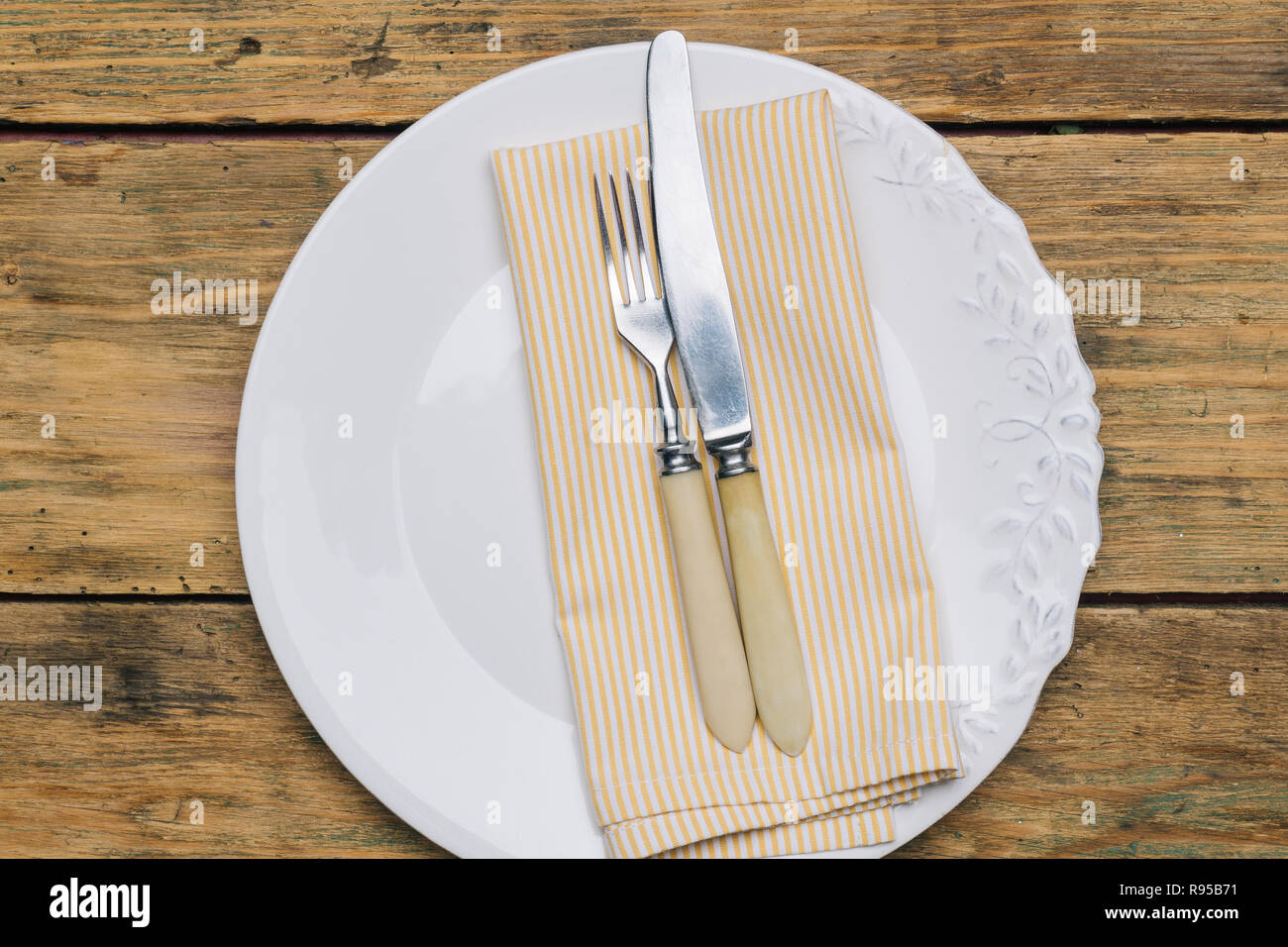 Empty white rustic plate on old wooden background with knife, fork and ...
