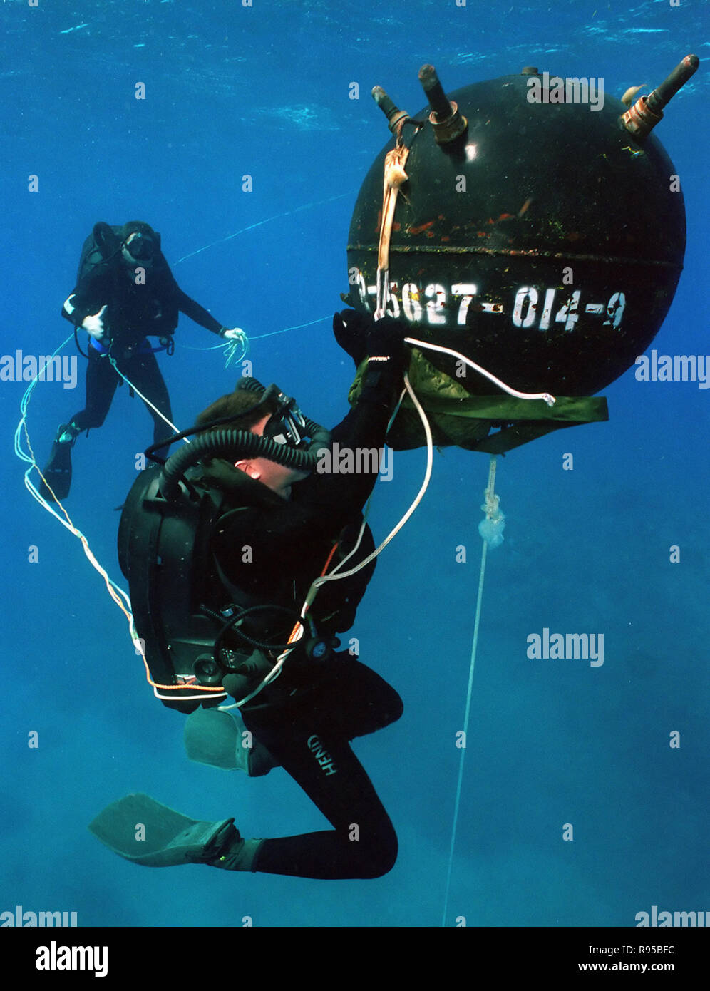 A U.S. Navy diver attaches an inert satchel charge to a training mine ...