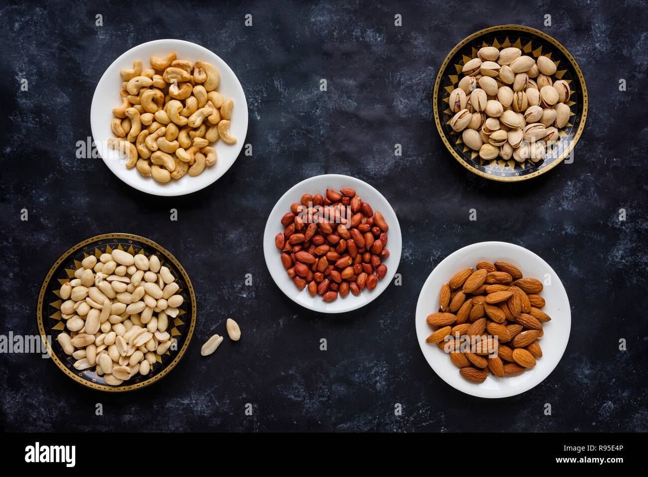 Individual dishes of assorted roasted fresh nuts on a dark background ...