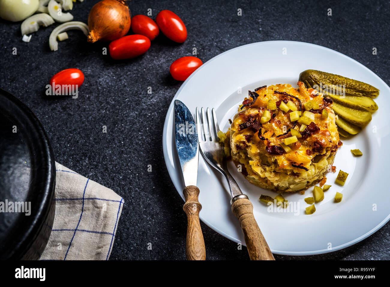 Gratin potatoes with onion and gherkin on white plate on black stone ...