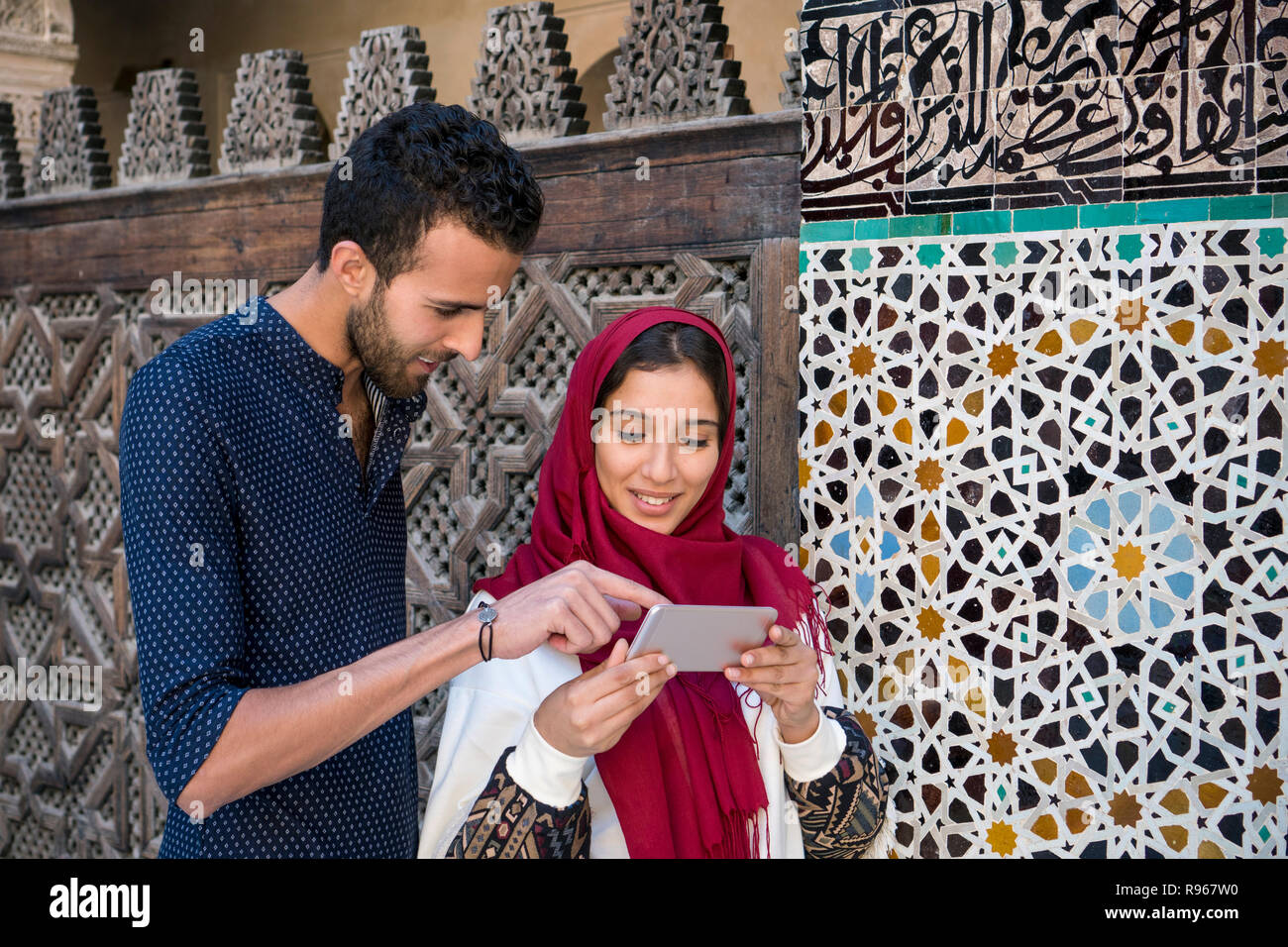 Smiling muslim couple looking at cellphone beside the arabesque ...