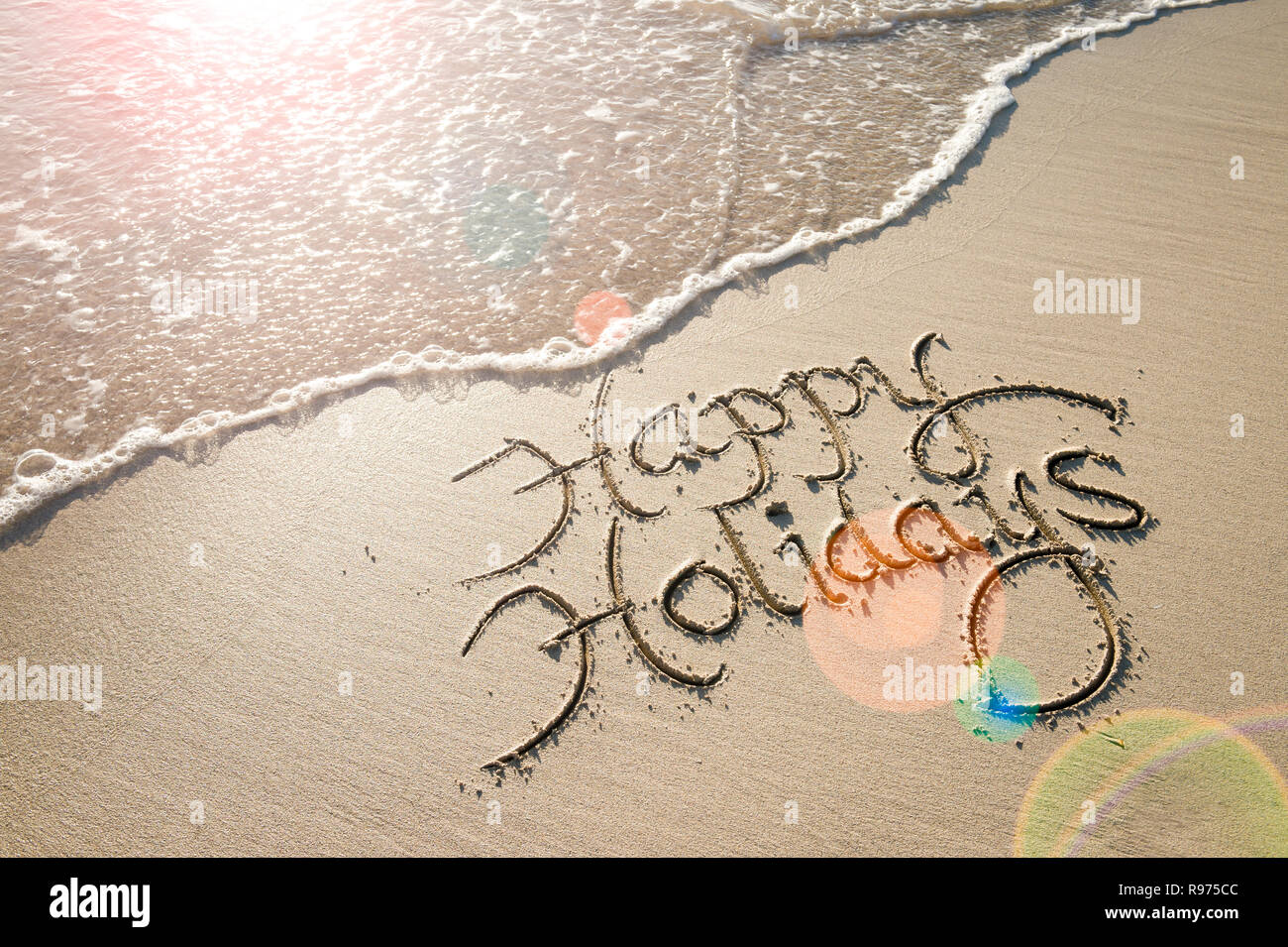 Happy Holidays message handwritten in smooth sand with an oncoming wave ...